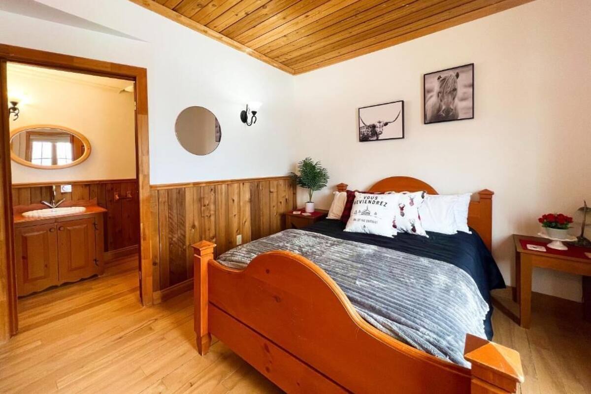 Quarto com teto de madeira, cama com cabeceira, mesa de cabeceira, espelho e obra de arte na parede.