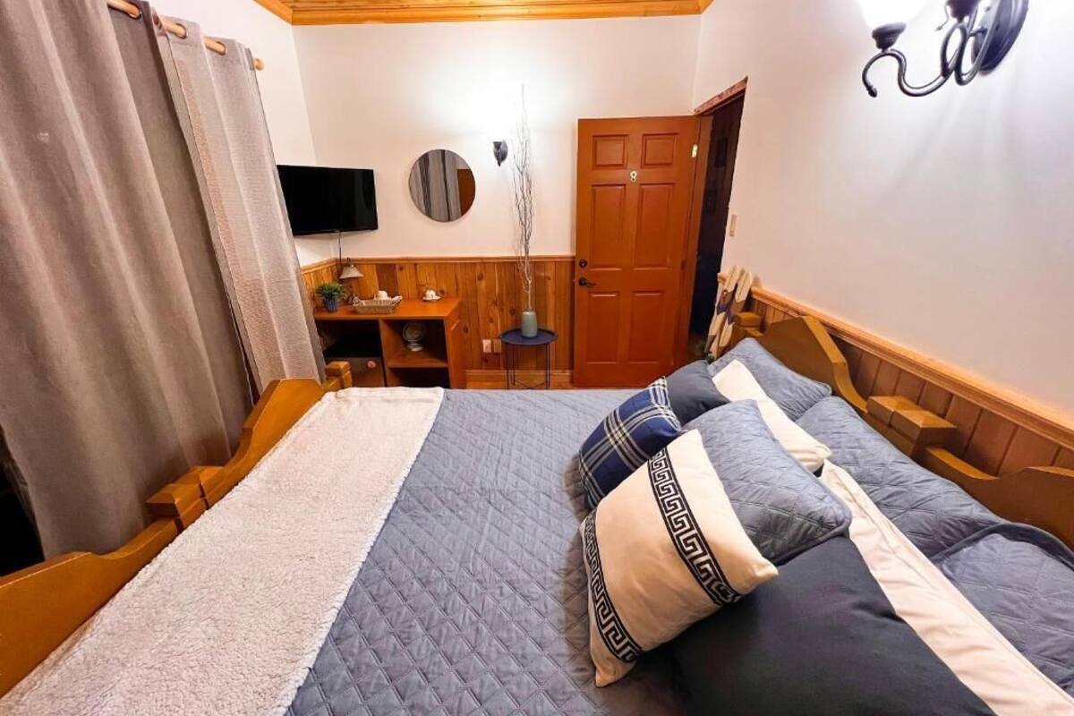 Quarto com cama, televisão, porta e luminária fixada na parede.