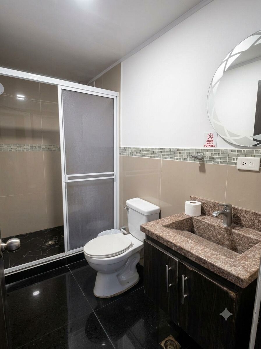Casa de banho com sanita, cabine de duche e lavatório com espelho.