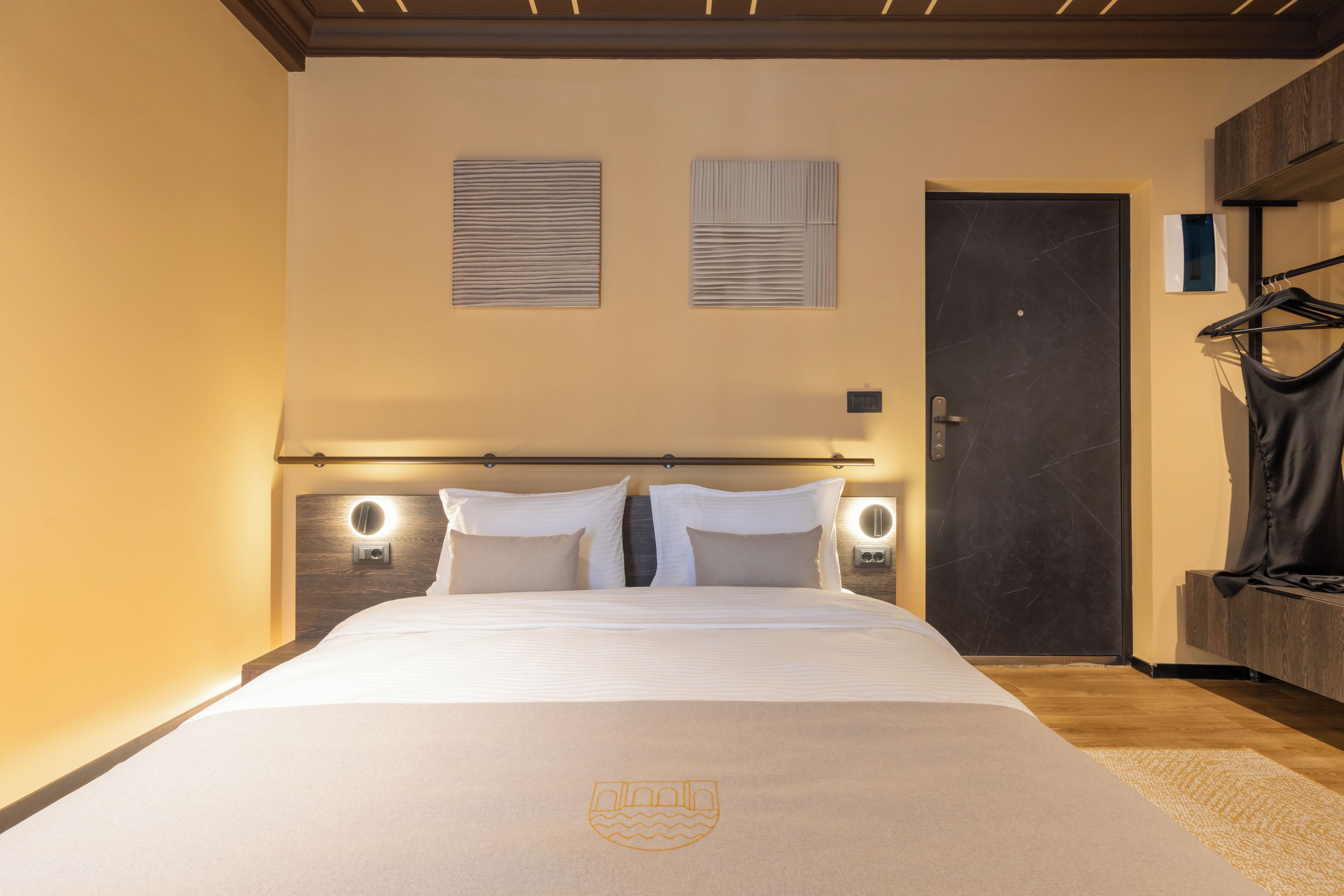 Quarto de hotel com uma cama, abajures, uma porta e um cabideiro.
