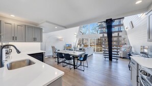 Uma cozinha moderna com armários cinzas, bancada branca e um espaço de jantar com mesa e cadeiras.