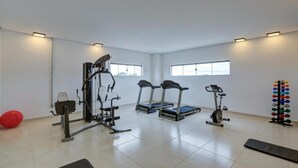 Uma academia com equipamentos de ginástica, esteiras, elíptico, uma bola de exercício vermelha e um suporte para halteres.