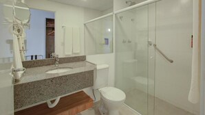 Uma casa de banho moderna com bancada de granito, lavatório branco, cabine de duche em vidro e sanita.