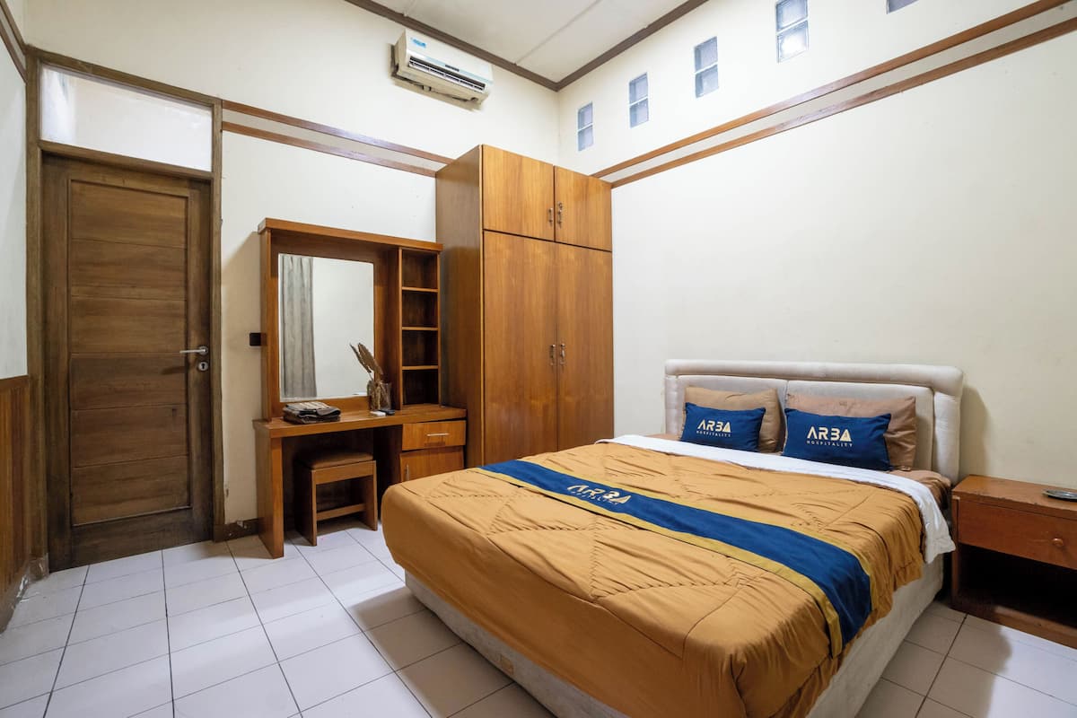 Quarto com cama, guarda-roupa de madeira, escrivaninha e espelho.