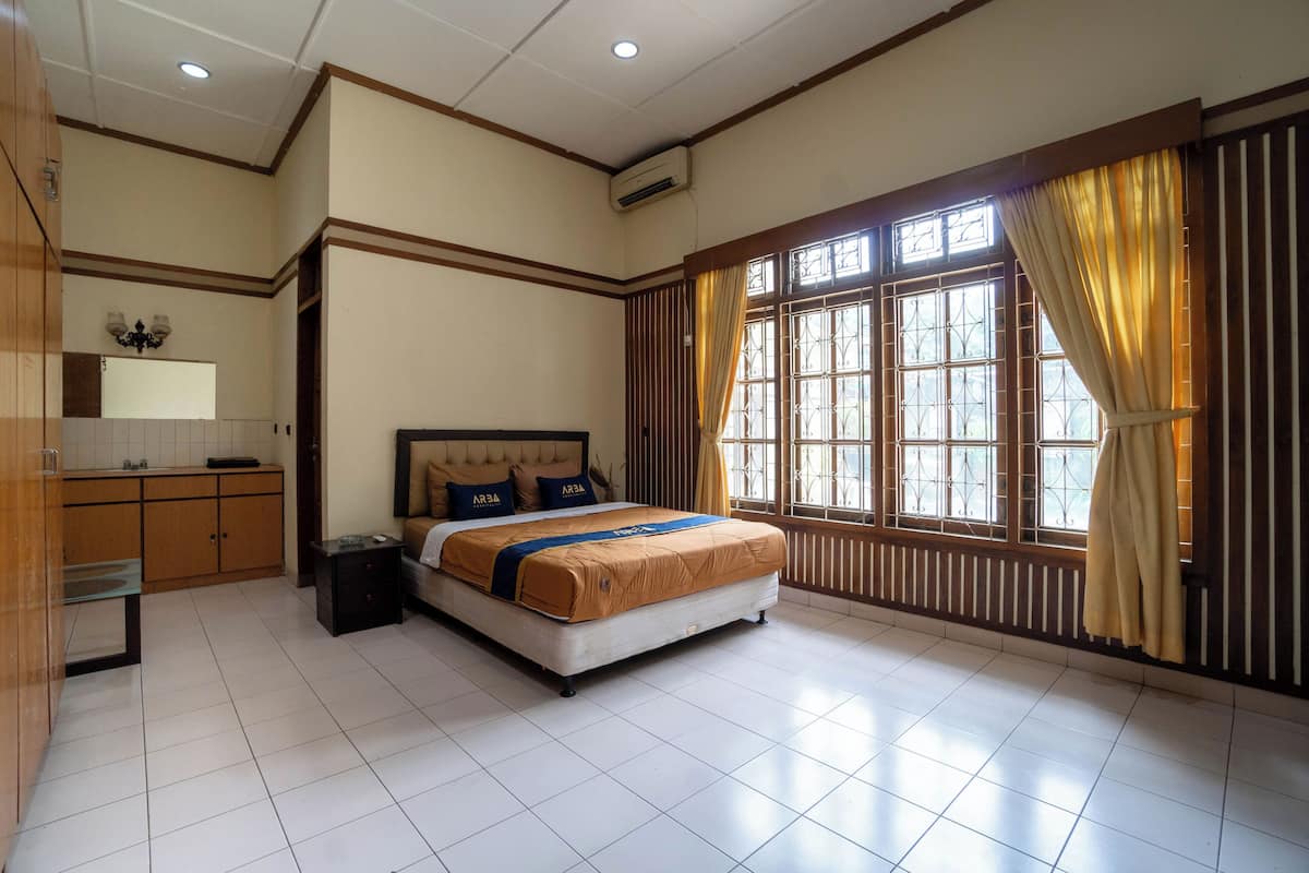 Quarto com cama, mesa de cabeceira, cômoda, espelho e janela com cortinas.