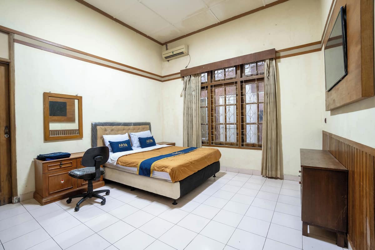 Quarto com cama, escrivaninha, cadeira, penteadeira e televisão fixada na parede.