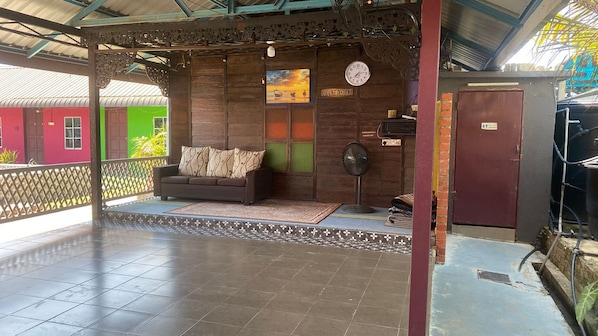 Uma área de estar coberta ao ar livre com sofá, relógio e ventilador.