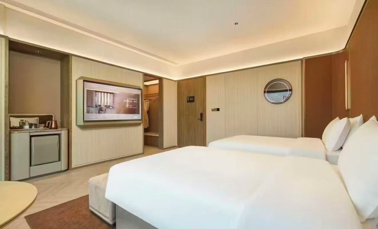 Quarto de hotel com duas camas, uma escrivaninha pequena, televisão e espelho.