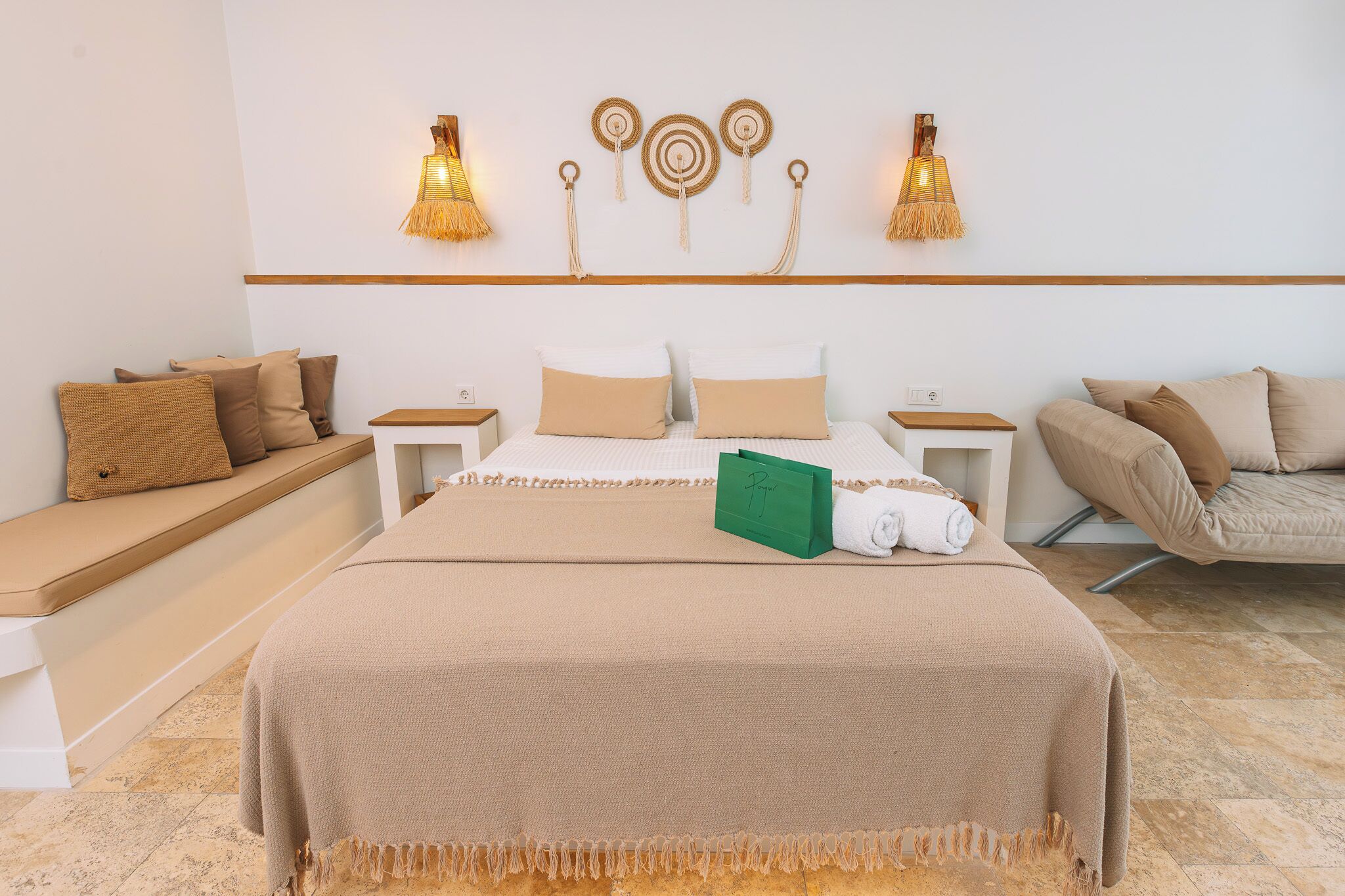 Quarto de hotel com cama, mesas de cabeceira, um banco e iluminação fixa na parede.