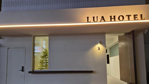 Exterior do HOTEL LUA com design moderno, entrada visível e uma pequena janela com vista para uma árvore.