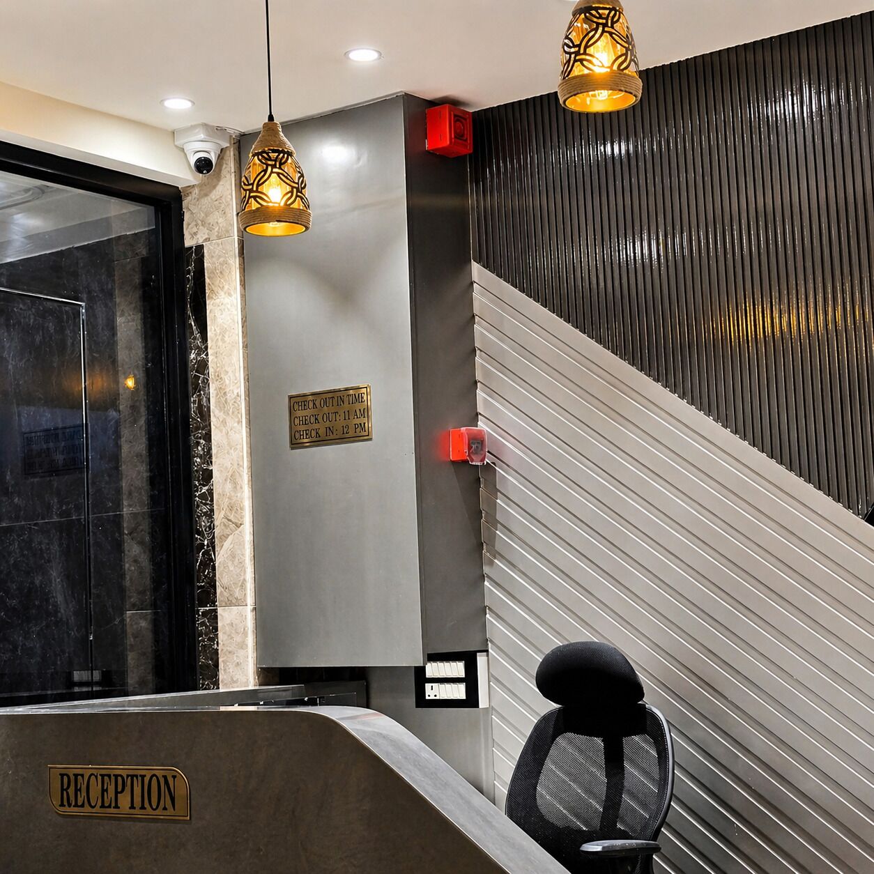 Uma área de recepção com placa de check-out, câmera de segurança e alarme de emergência vermelho.