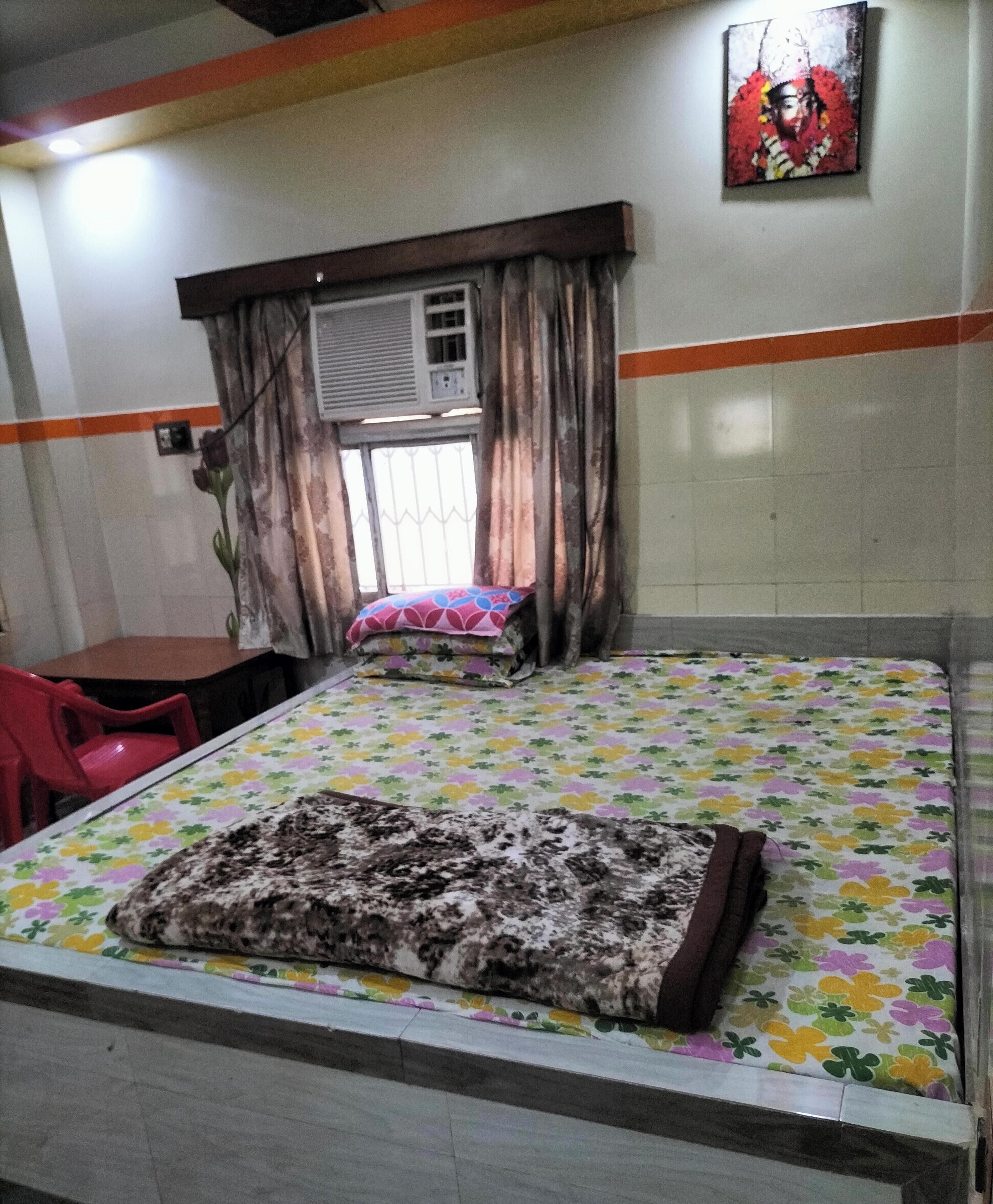 Quarto com cama, janela com cortinas, ar-condicionado fixado na parede e uma cadeira vermelha.