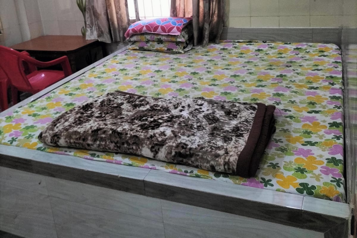 Quarto com cama, janela com cortinas, ar-condicionado fixado na parede e uma cadeira vermelha.