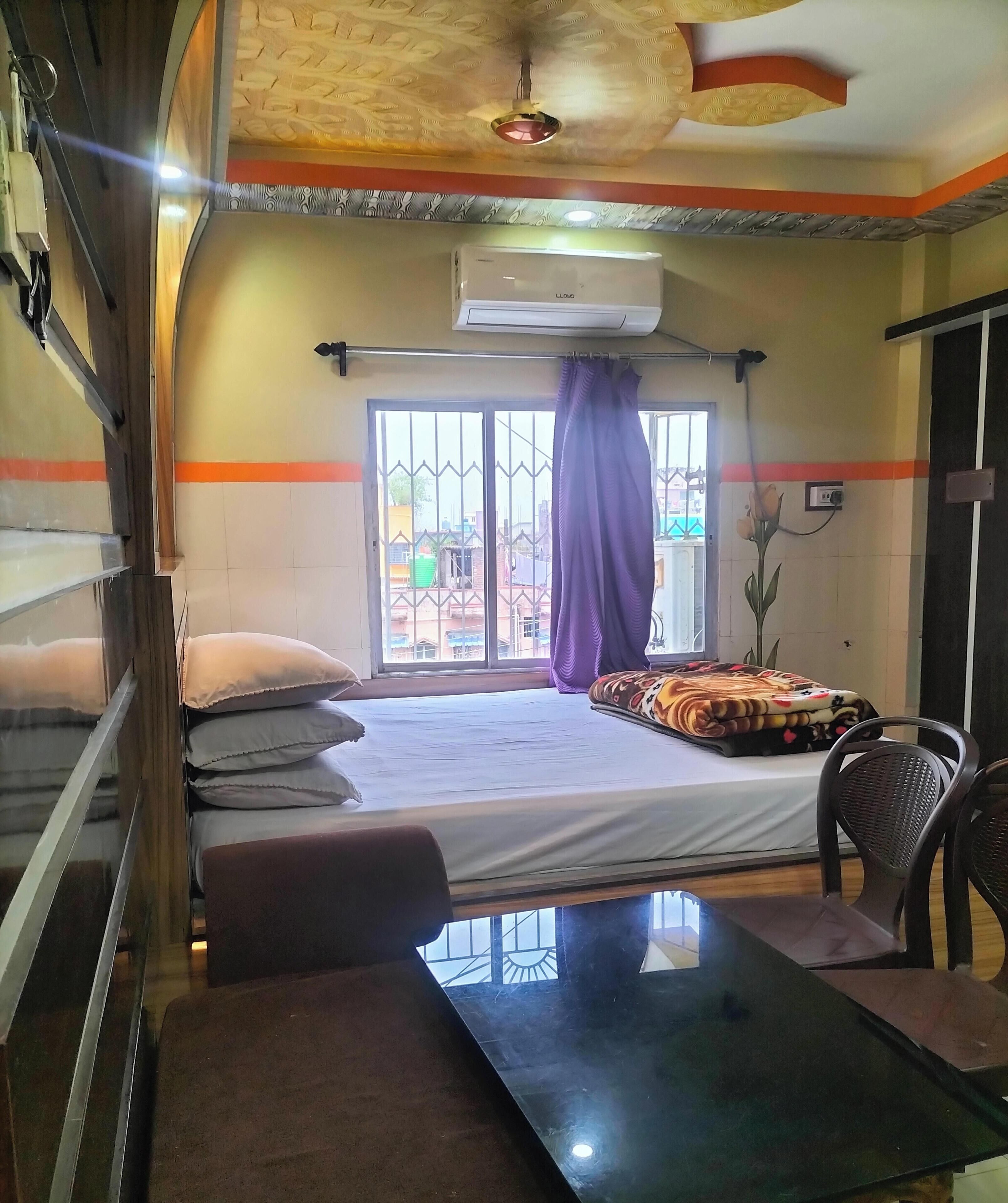 Quarto com cama, mesa, cadeira, aparelho de ar condicionado e janela com cortina.