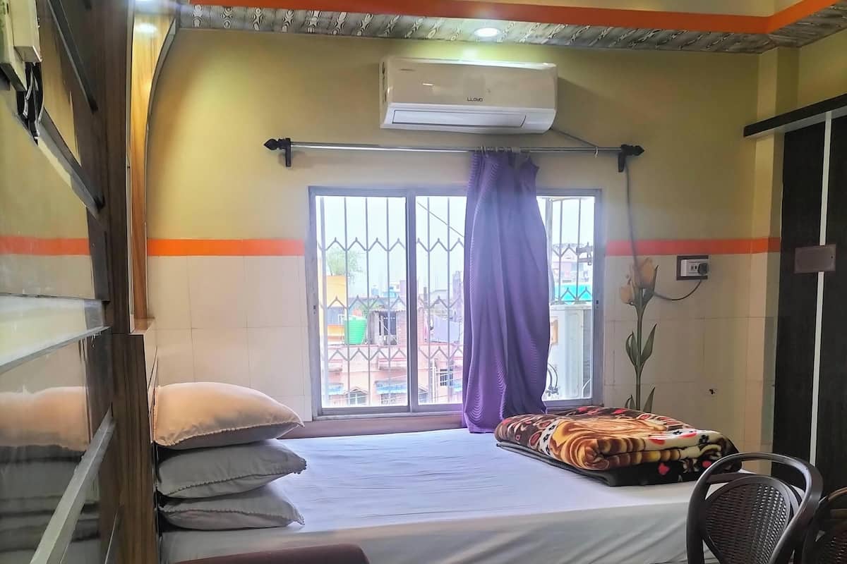 Quarto com cama, mesa, cadeira, aparelho de ar condicionado e janela com cortina.