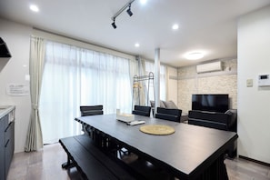 Uma sala de jantar moderna com uma mesa comprida, cadeiras, uma televisão e um aparelho de ar condicionado.