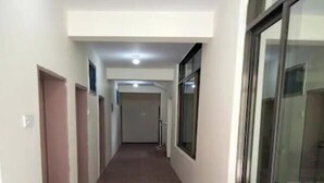 Um corredor longo e estreito, com piso de madeira, paredes brancas e uma porta de vidro à direita.