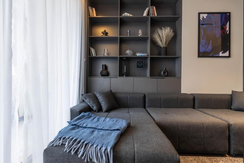 Uma sala de estar moderna com um sofá modular cinza, uma estante com diversos objetos decorativos e uma pintura abstrata emoldurada na parede.