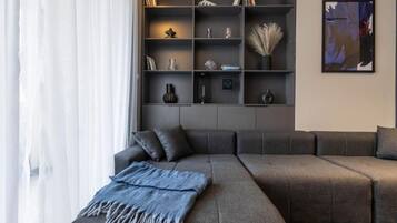 Uma sala de estar moderna com um sofá modular cinza, uma estante com diversos objetos decorativos e uma pintura abstrata emoldurada na parede.