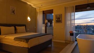Quarto com cama, banheira, vista para a cidade e porta que dá para uma varanda.
