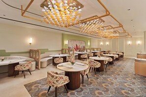 Um espaço de refeições de hotel com mesas redondas, cadeiras florais e um tapete estampado.