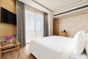 Quarto de hotel com uma cama grande, televisão de tela plana na parede, mesa de cabeceira de madeira com um vaso de flores e guarda-roupa de madeira.