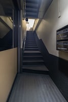 Uma escadaria em um edifício, com corrimão, prateleira na parede e uma porta no topo.
