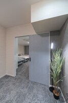 Quarto de hotel com carpete cinza, uma planta em vaso e uma cama com roupa de cama cinza.