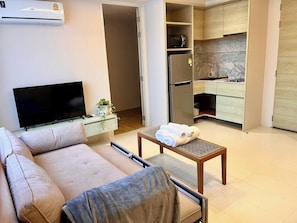 Espaço compacto com sofá, TV, mesa pequena e cozinha compacta.