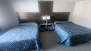 Quarto de hotel com duas camas, uma mesa de cabeceira e uma luminária fixada na parede.