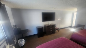 Quarto de hotel com cama, escrivaninha, cadeira, televisão e luminária.