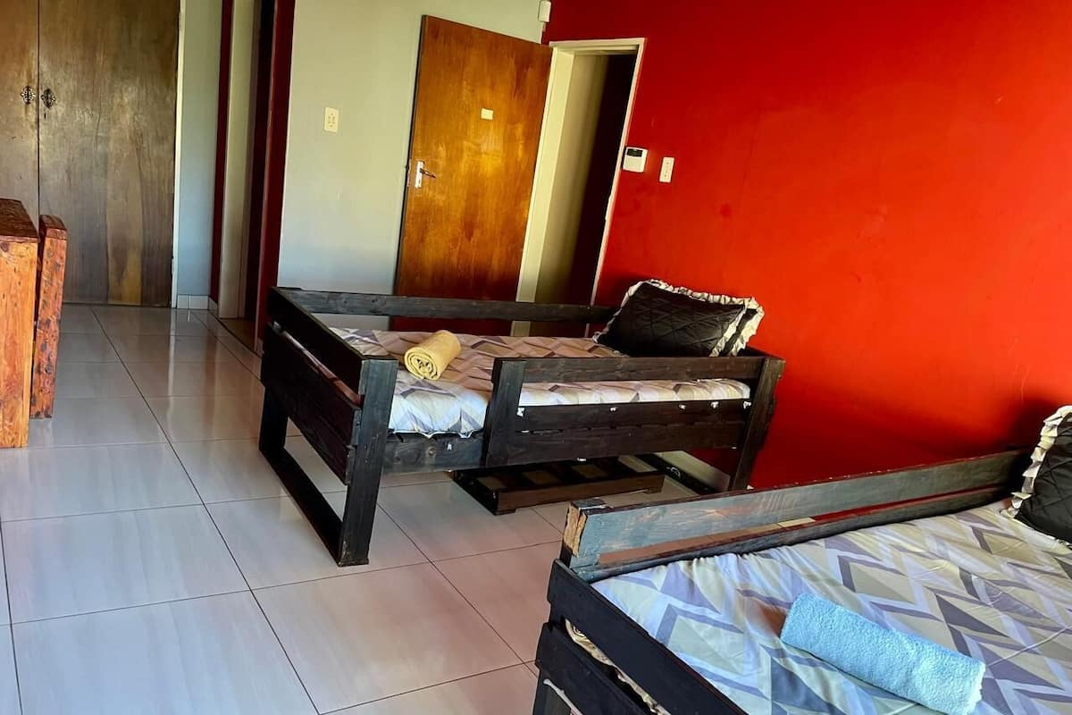 Quarto com duas camas de madeira, parede vermelha e porta de madeira.