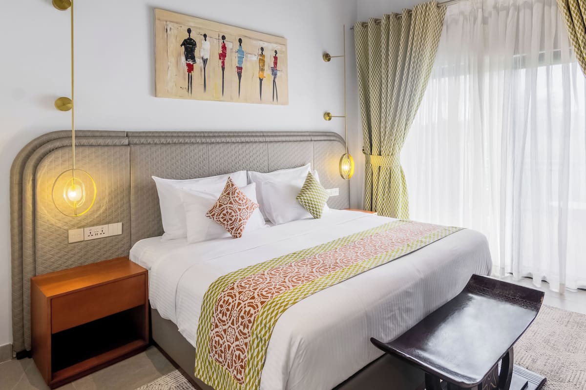 Quarto de hotel bem arrumado, com uma cama, mesa de cabeceira, abajur e uma obra de arte na parede.