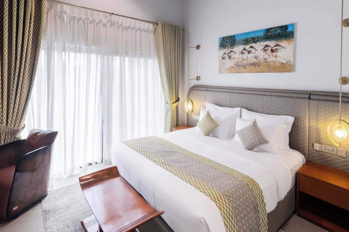 Quarto de hotel com uma cama grande, uma escrivaninha, uma cadeira e um quadro na parede.