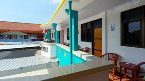 Uma área externa coberta com um balcão, cadeiras e um edifício com telhado vermelho ao fundo.
