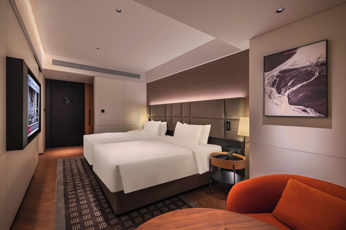 Quarto de hotel com uma cama grande, uma escrivaninha, uma cadeira, uma televisão e um quadro na parede.
