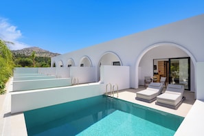 Uma área de piscina moderna com água azul cristalina, paredes brancas e janelas em arco.