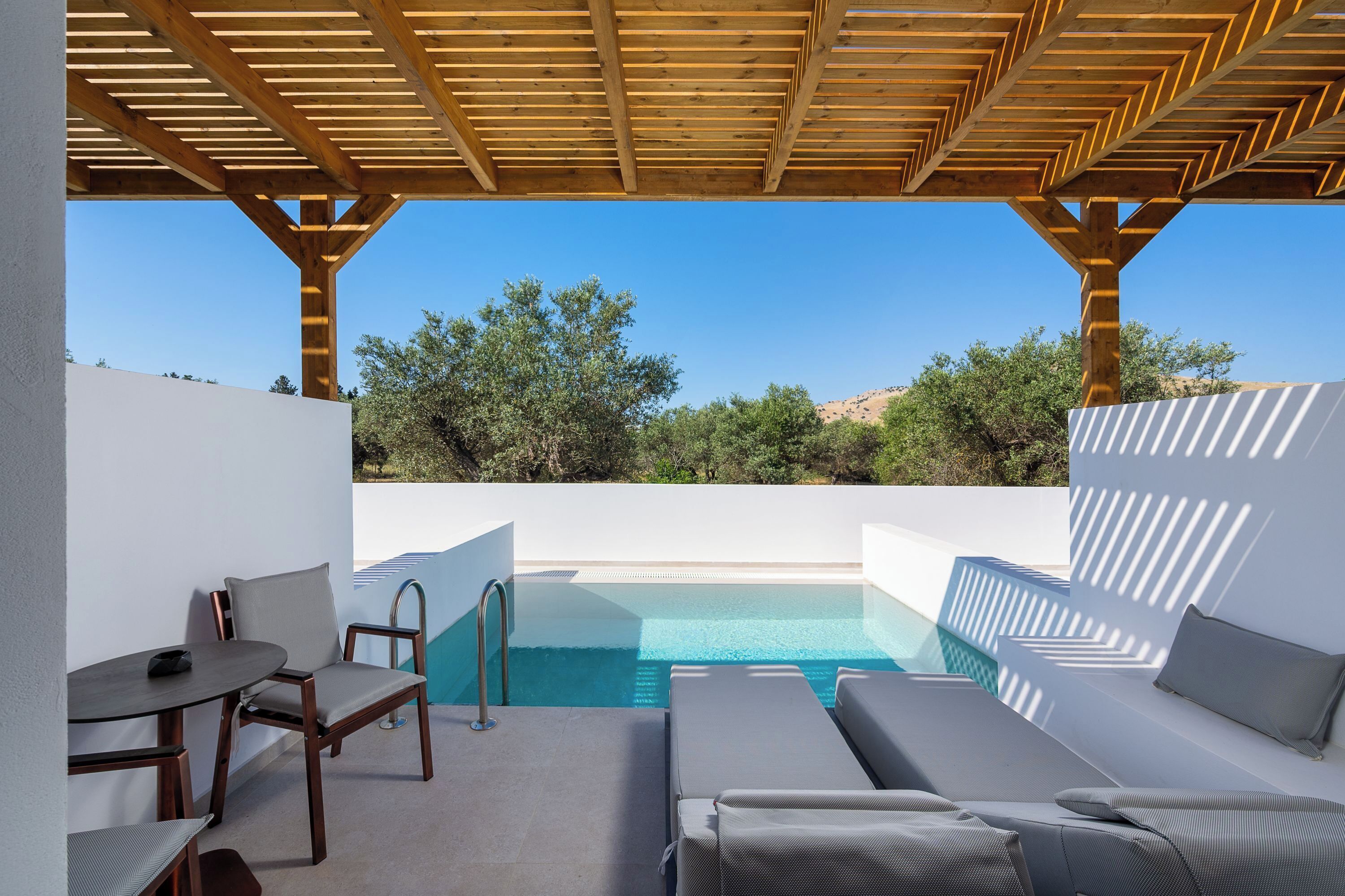 Uma área de piscina com pérgola de madeira, espreguiçadeiras e uma mesa.