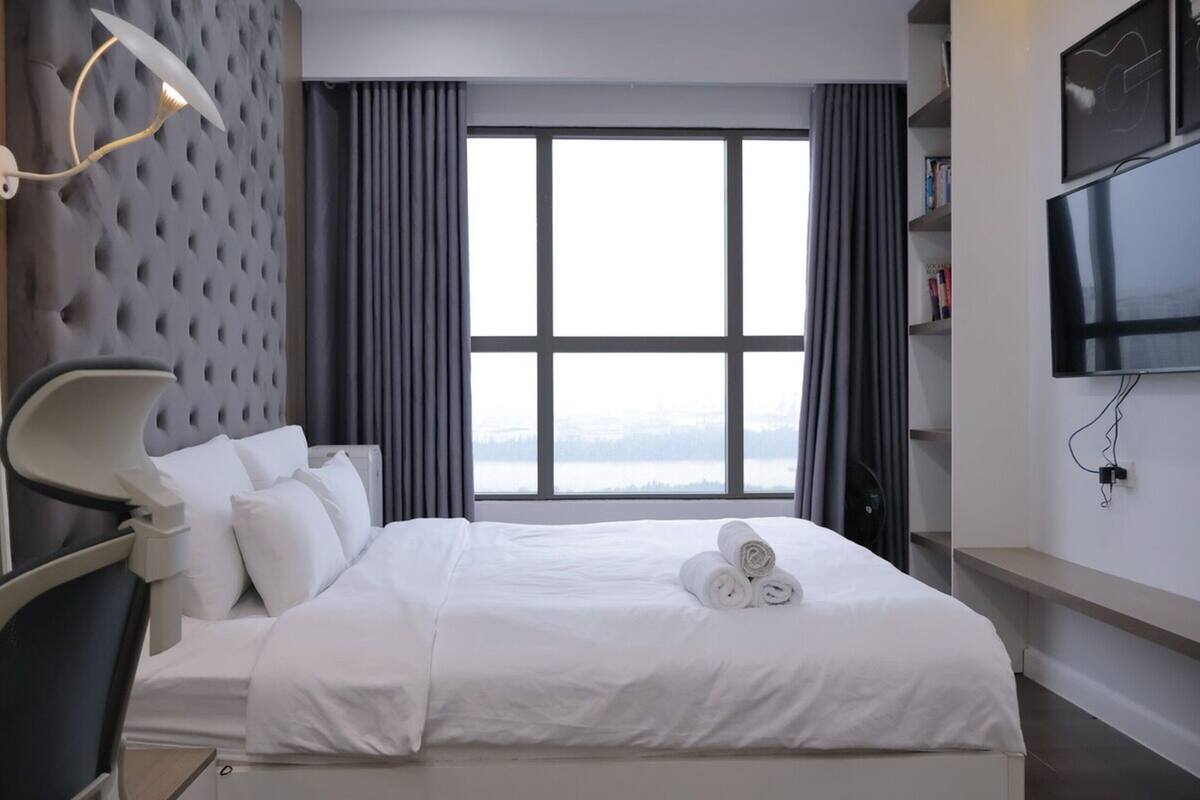 Quarto de hotel moderno com uma cama grande, cabeceira com textura, TV na parede e vista para o exterior através de uma janela ampla.