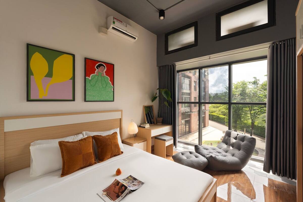 Quarto de hotel moderno com uma cama grande, uma mesa, uma cadeira e varanda com vista.