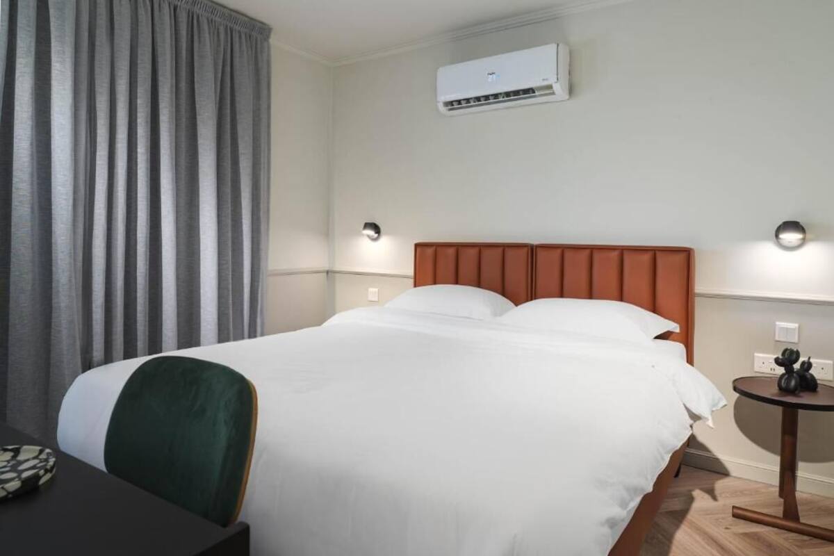 Quarto de hotel com cama, mesa de cabeceira, luminária, aparelho de ar condicionado e cortina.