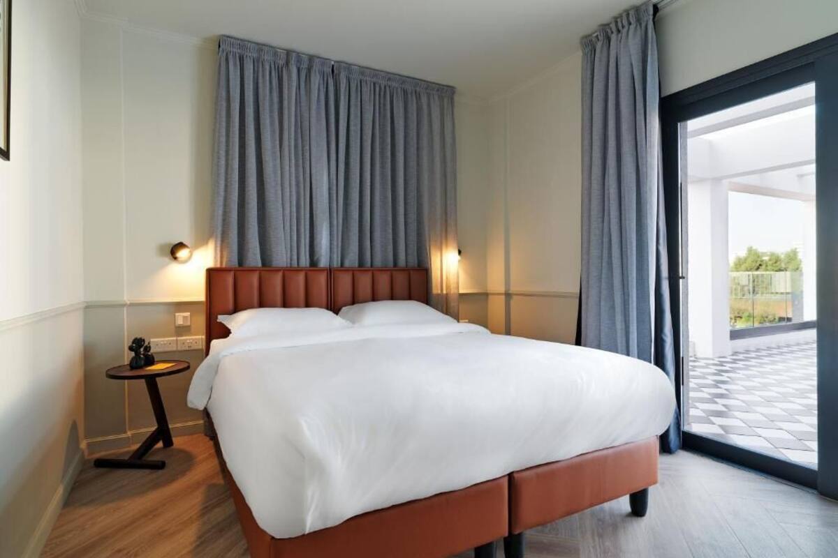 Quarto de hotel com uma cama grande, mesa de cabeceira, abajur e vista para o exterior.
