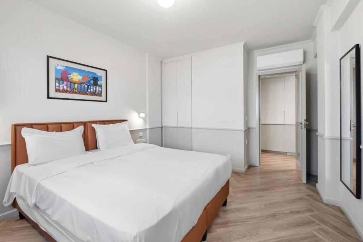 Um quarto com cama, mesa de cabeceira, guarda-roupa e uma porta que dá para outro cômodo.