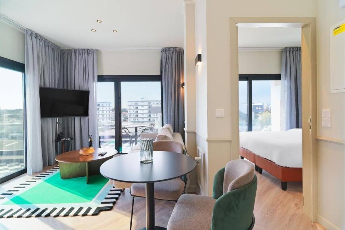Quarto de hotel com cama, televisão, mesa de jantar e vista da cidade.