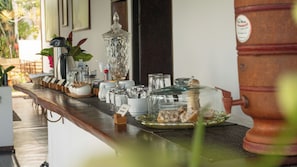 Uma mesa de pequeno-almoço com diversos alimentos, uma máquina de café e um recipiente de vidro decorativo.