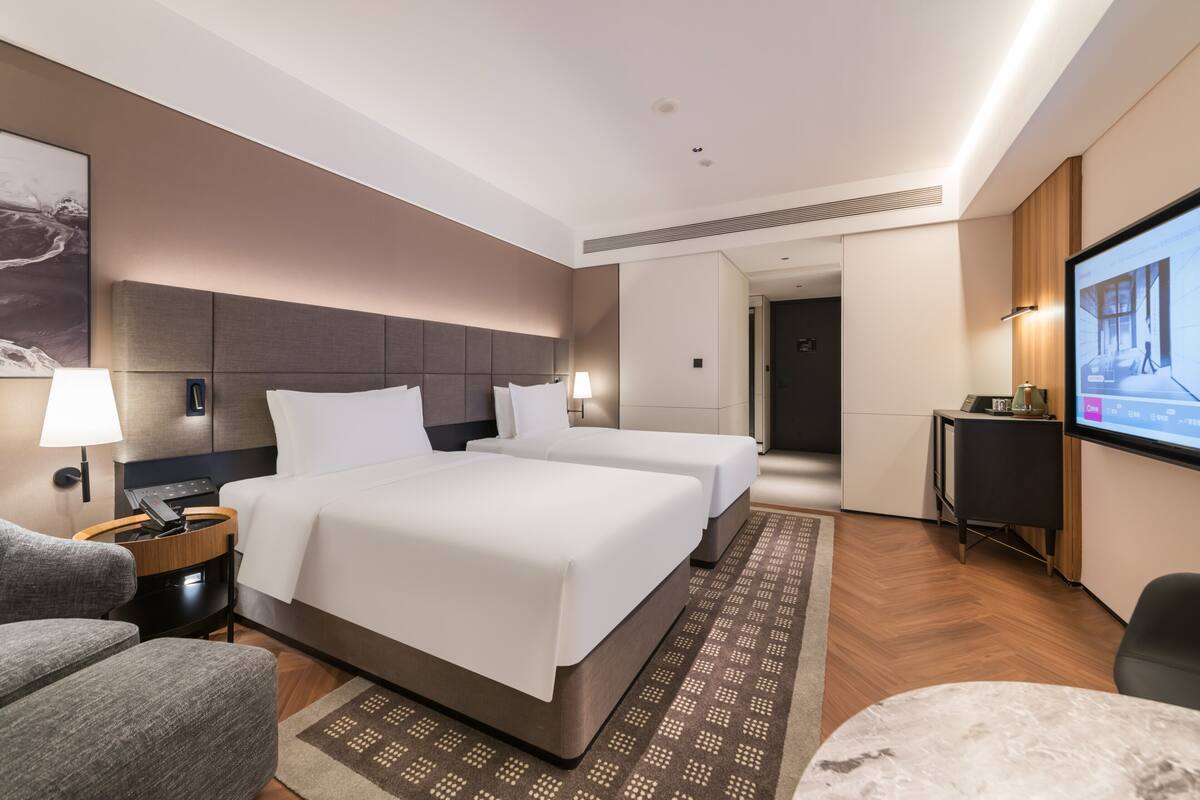 Quarto de hotel com uma cama grande, duas mesas de cabeceira, uma televisão, uma escrivaninha e uma cadeira.
