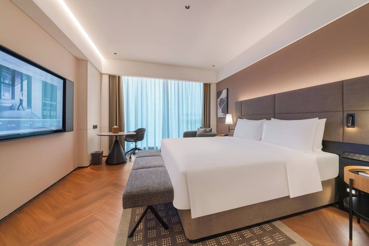 Quarto de hotel moderno com uma cama grande, uma escrivaninha, uma cadeira e televisão na parede.