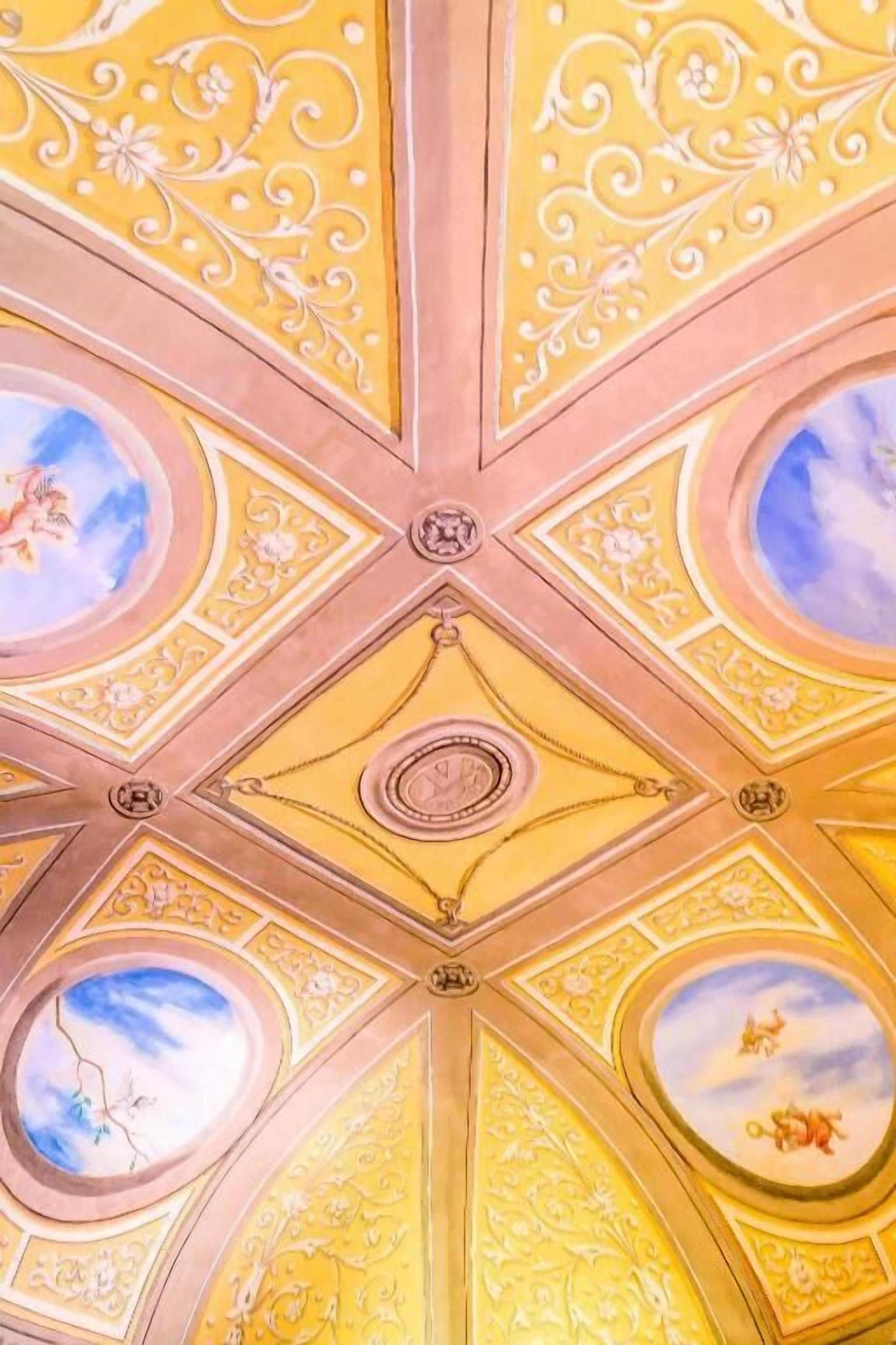 Teto com intrincados padrões dourados e cor-de-rosa, claraboias circulares e uma medalhão central.