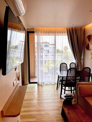 Uma sala de estar moderna com televisão de tela plana na parede, uma área de jantar com mesa e cadeiras, e um sofá.
