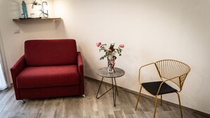 Um sofá vermelho, uma mesa redonda com um vaso de flores e uma cadeira de arame num quarto com soalho de madeira.
